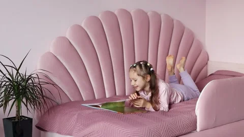 A little girl is lying on the bed lookin... | Stock Video | Pond5