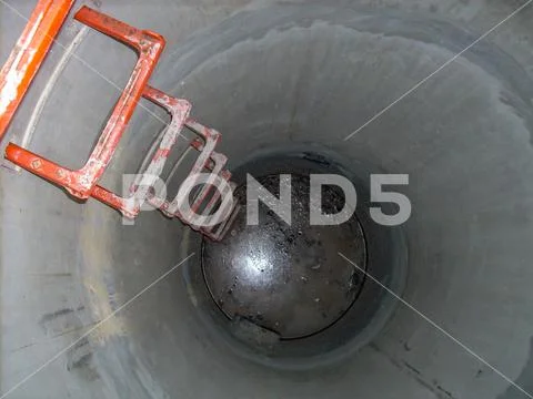 Looking into an open concrete manhole with step rungs leading down ...
