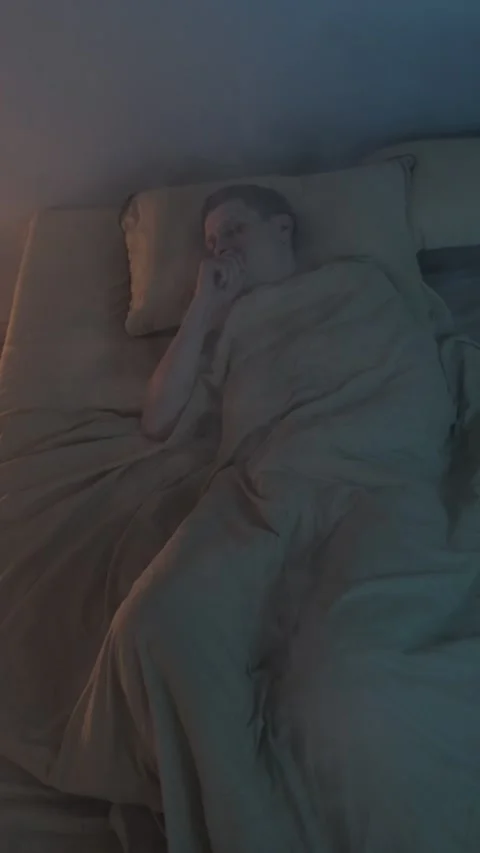 A man lies in bed under covers, coughing... | Stock Video | Pond5
