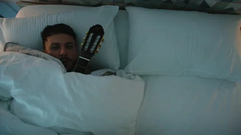 Man sing and Play the guitar in a bed | Stock Video | Pond5