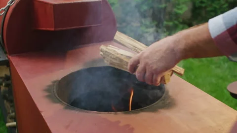 man's hand tosses firewood in the smoker | Stock Video | Pond5