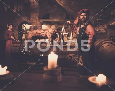 Medieval man doing roasted pig on the rack in ancient castle kitchen ...