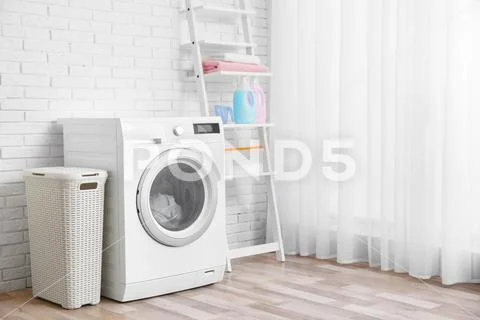 Photograph: Modern washing machine near brick wall in laundry room ...