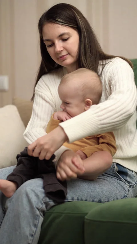mom puts clothes on baby son sitting on ... | Stock Video | Pond5