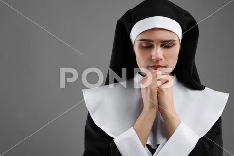 Nun with clasped hands praying to God on grey background. Space for ...