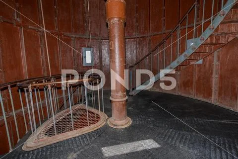 Old lighthouse on the inside. Red iron spiral stairs, round window and ...