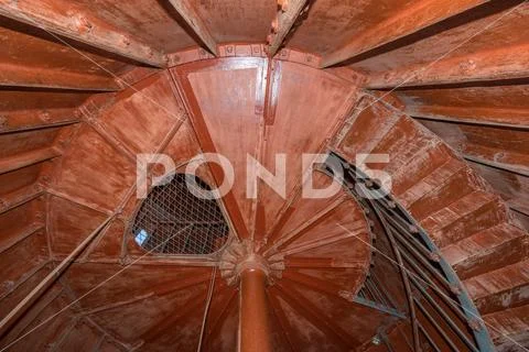 Old lighthouse on the inside. Red iron spiral stairs, round window and ...