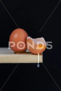 One whole and one half an egg stands on the edge of a wooden table. The ...