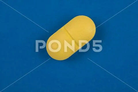 Oval shaped yellow pill in macro view isolated on blue background ~ Hi ...