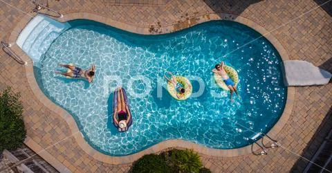 Overhead view of family floating in a swimming pool on summer day ...