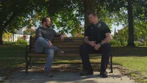 Police Man Talks With Friend On Park Ben... | Stock Video | Pond5