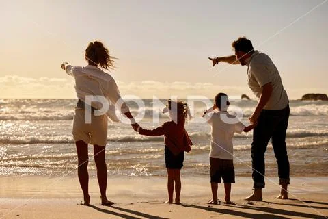 Rear view of family on holiday at the beach during sunset. Mother and ...