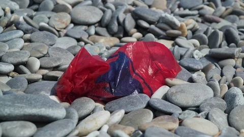 Red plastic bag littering a pebble beach... | Stock Video | Pond5