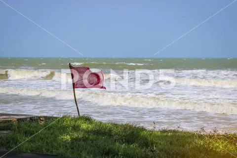 Red warning flag flapping in the wind on beach at stormy weather ...