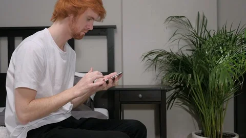 Redhead Man Sitting on Side of Bed Using... | Stock Video | Pond5