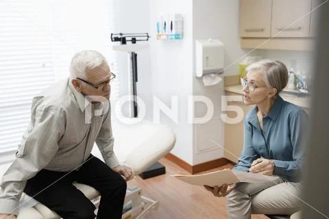 Senior doctor and patient discussing medical chart in clinic exam room ...