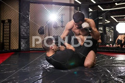 Shirtless muscular mma fighter in boxing gloves sitting above opponent ...