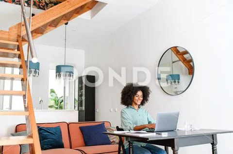 Side view of black woman sitting with laptop computer at the table at ...