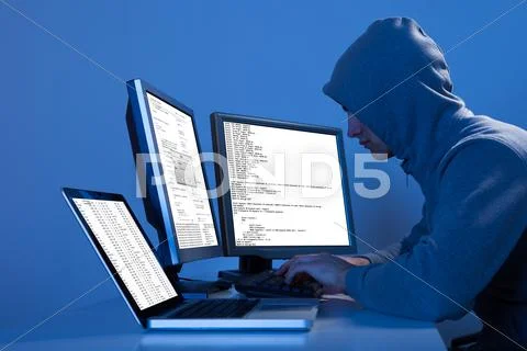 Side view of hacker using multiple computers to steal data at table ...
