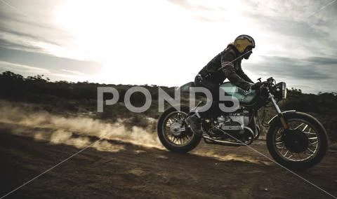 Side view of man wearing crash helmet riding cafe racer motorcycle on a ...