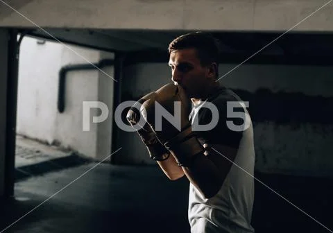 Photograph: Side view of muscular young man boxing with punching bag ...