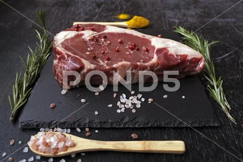 Side view raw rib eye steak on a square black slate board with two ...