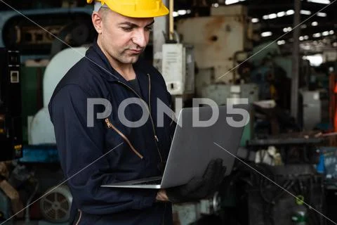 Skillful factory worker working with laptop computer to do procedure ...