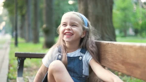 Small happy child girl sitting on a benc... | Stock Video | Pond5