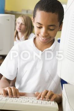 Student at computer terminal typing with student in background ...