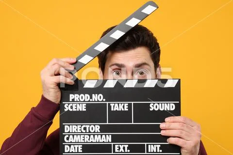 Photograph: Surprised actor holding clapperboard on orange background ...