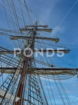 Tall mast of an old sailing ship with a ship's cable ladder in the blue ...