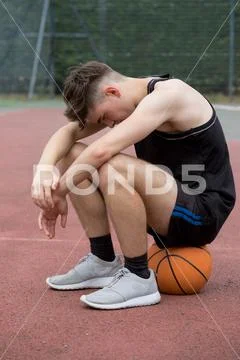 Teenage boy sitting on a basketball on a court looking sad ~ Hi Res ...