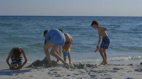 Tween girl helps little boys dig in sand... | Stock Video | Pond5