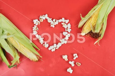 Two corns and popcorn shaped like heart on red background ~ Hi Res ...