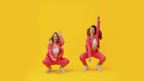 Two girls dancing on yellow background | Stock Video | Pond5
