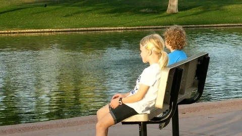 Two Kids Sitting on Park Bench by Duck P... | Stock Video | Pond5