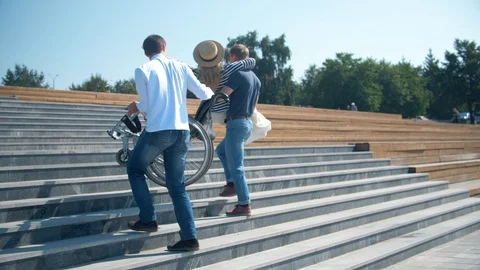 Two men carry a woman in a wheelchair on... | Stock Video | Pond5