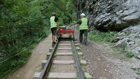 Two workers push a work cart along a nar... | Stock Video | Pond5