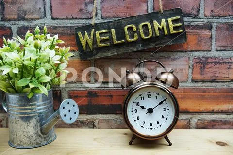 Photograph: Welcome sign hanging with alarm clock on old brick wall ...
