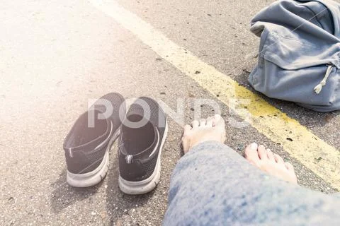 Photograph: Woman with bare feet and backpack sitting on an asphalt ...