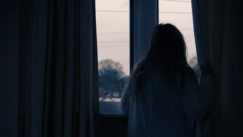 Woman looking out of window in dark room | Stock Video | Pond5