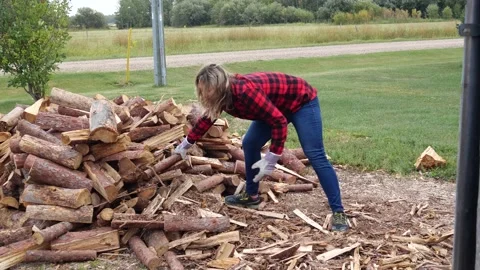 Woman picking up logs from a pile and th... | Stock Video | Pond5