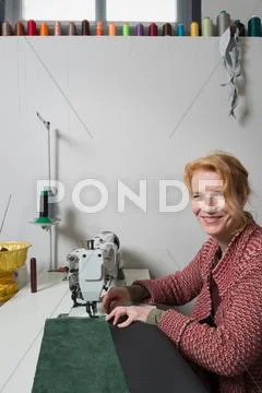 Woman at sewing machine looking at camera smiling ~ Hi Res #64160148
