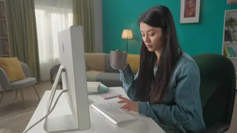 A woman sits at a computer and drinks mo... | Stock Video | Pond5