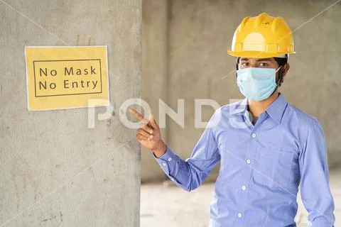 Worker pointing No Mask No Entry signage notice board on wall at ...
