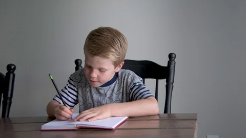 A young boy sitting down at a table whil... | Stock Video | Pond5