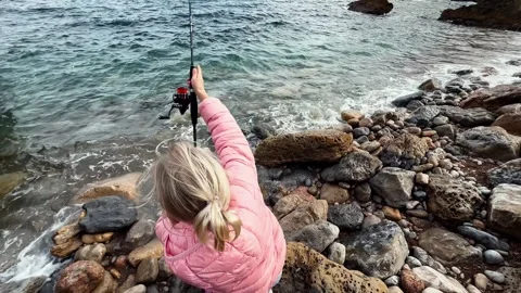 Young girl fishing from rocks by the sea... | Stock Video | Pond5