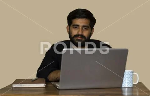 Photograph: A young indian man looking at the camera while working on ...