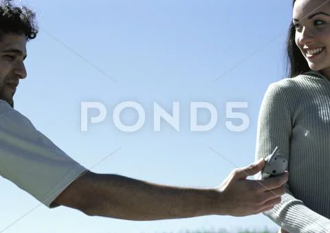 Young man handing cell phone to young woman with sky in background ...