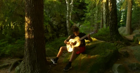 Young man playing guitar in forest and r... | Stock Video | Pond5